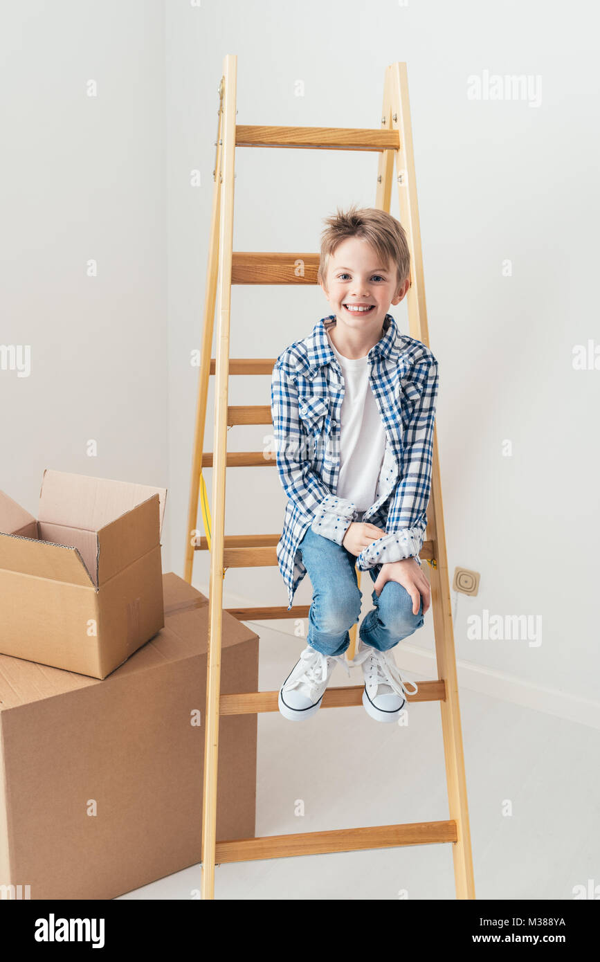 Cute young boy sitting on a ladder and smiling at camera, home ...