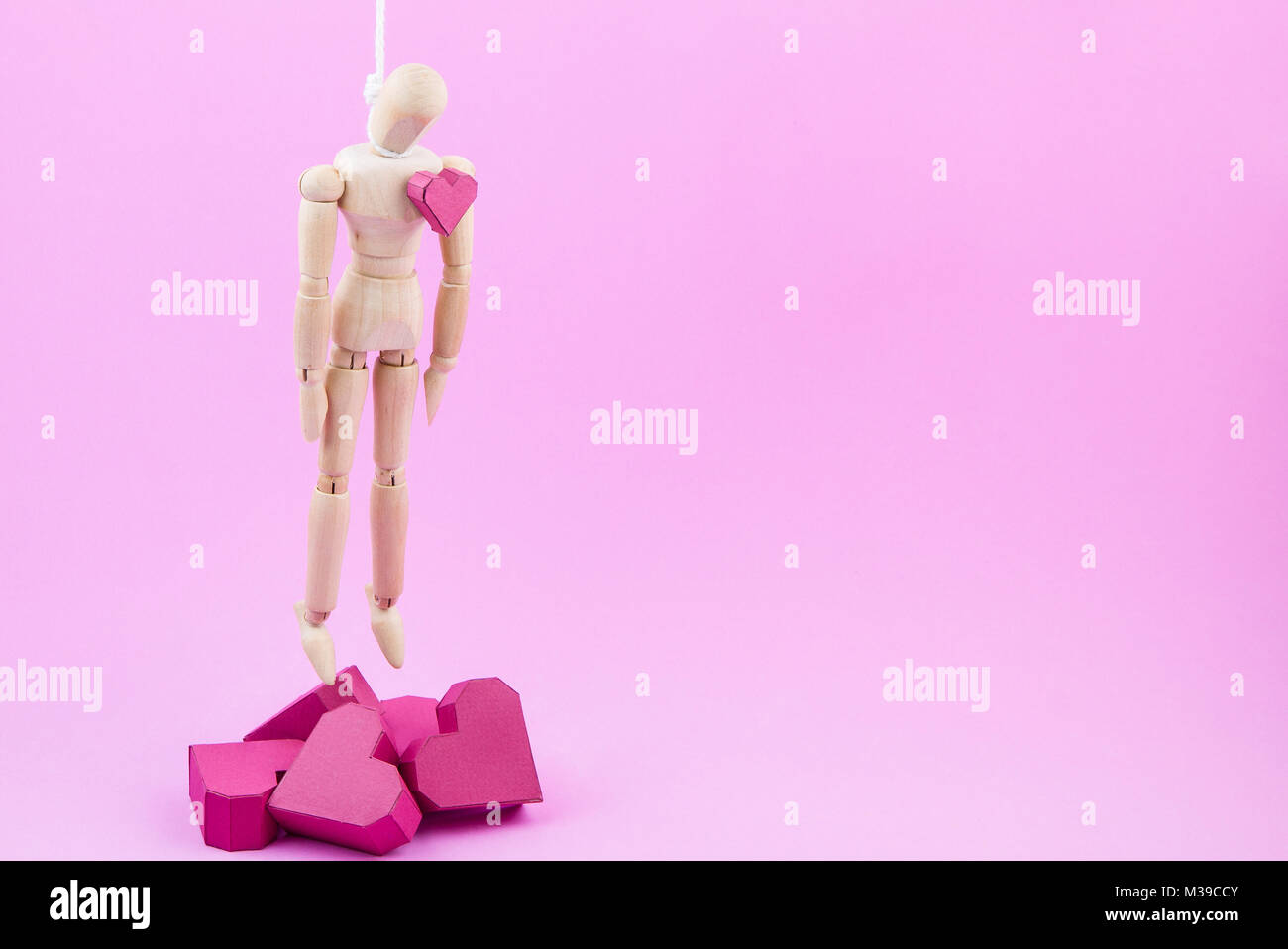 Wooden dummy hanged himself on a pile of paper box red heart shape on ...