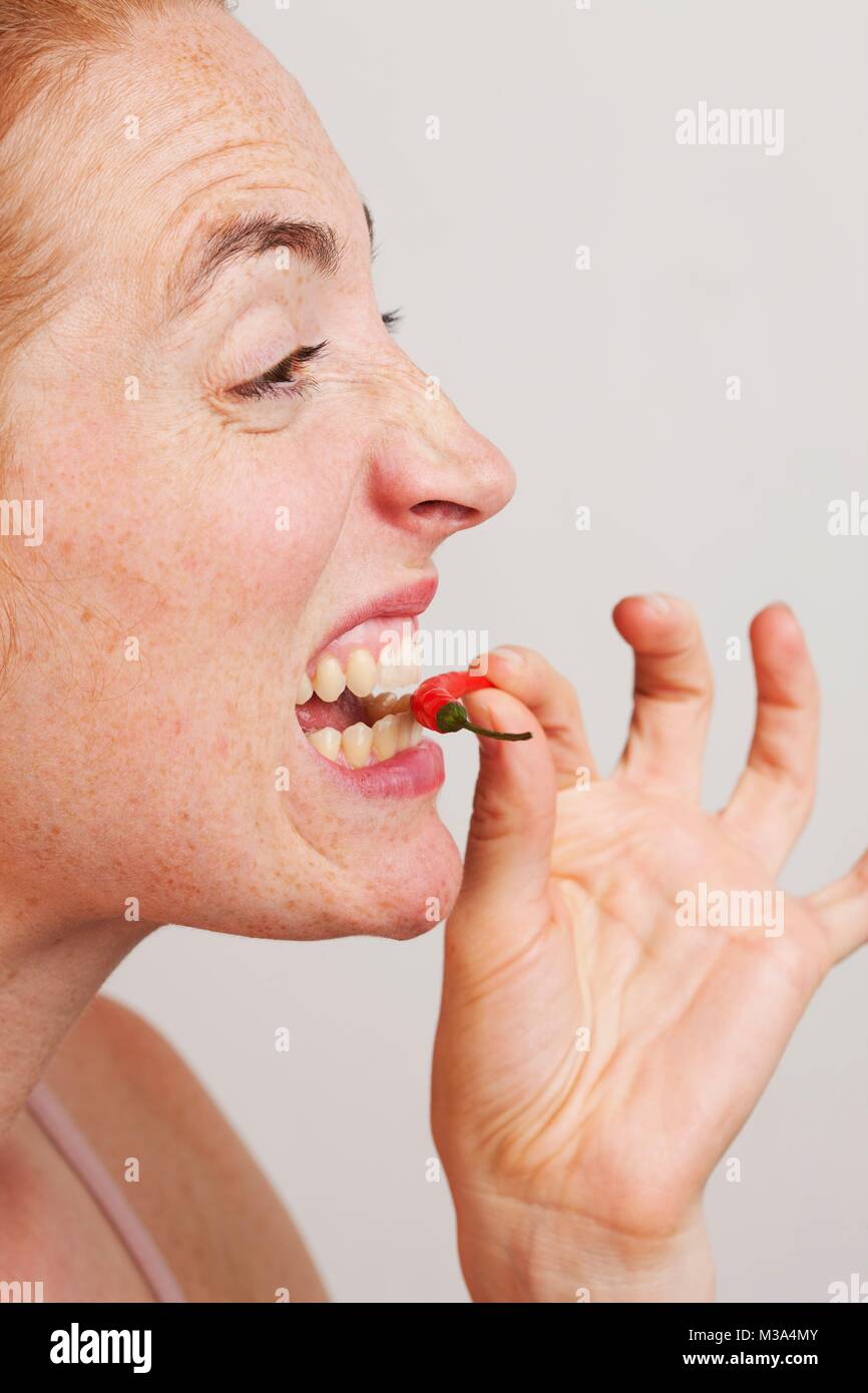 MODEL RELEASED. Profile of woman biting into red chili Stock Photo - Alamy