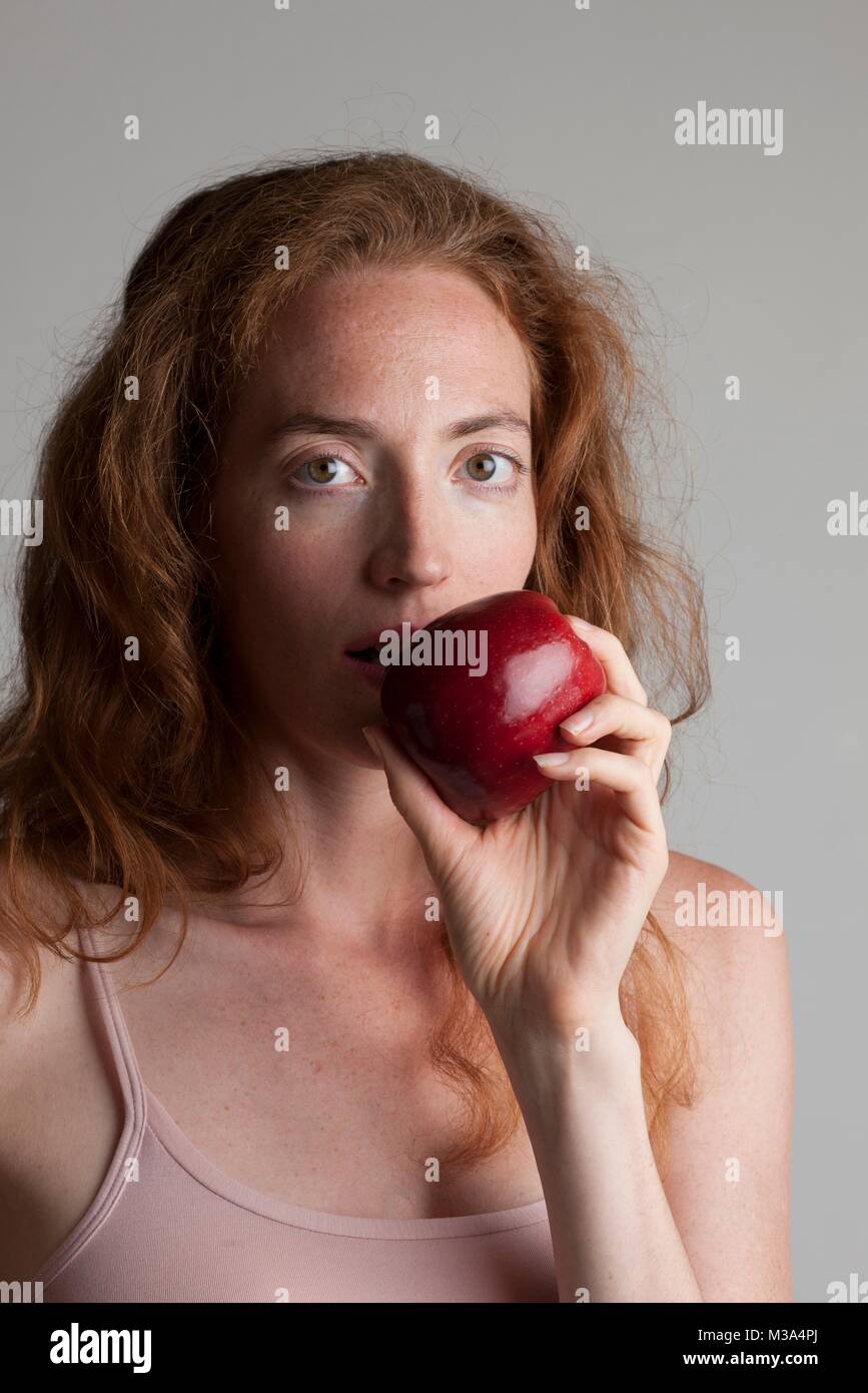 MODEL RELEASED. Portrait of woman eating red apple as part of a healthy ...