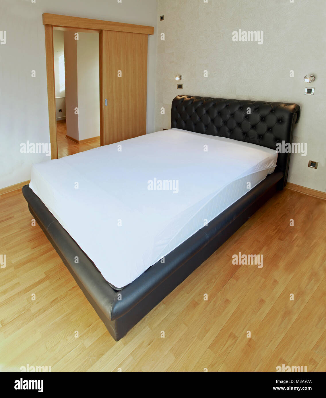 Large leather double bed in empty bedroom Stock Photo - Alamy
