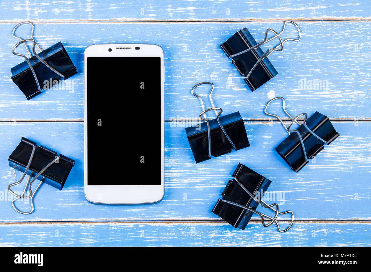 Black Binder Clips on blue wooden background with smartphone and copy ...