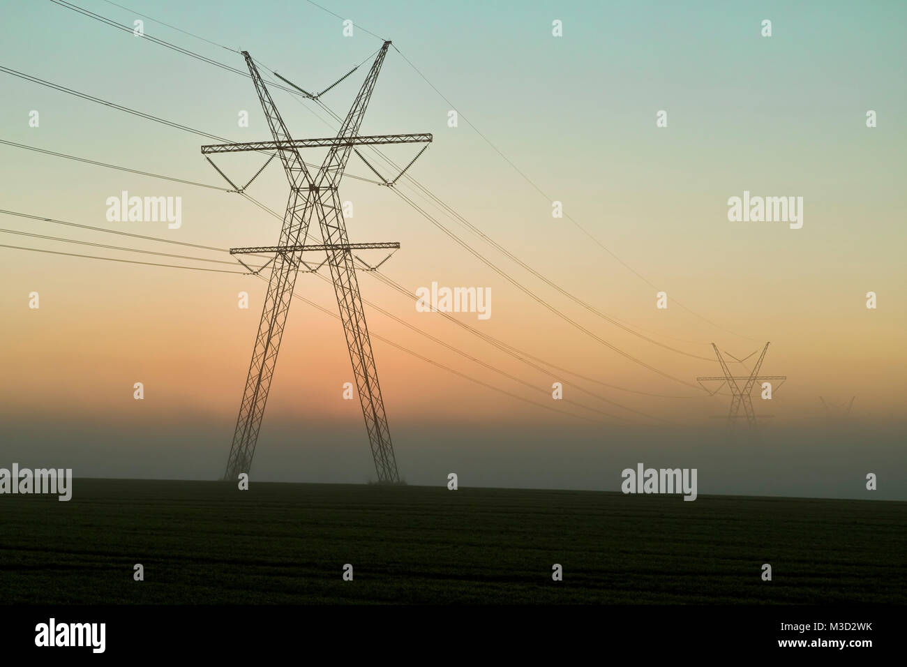 Power pylons in the sunset on a misty evening Stock Photo - Alamy