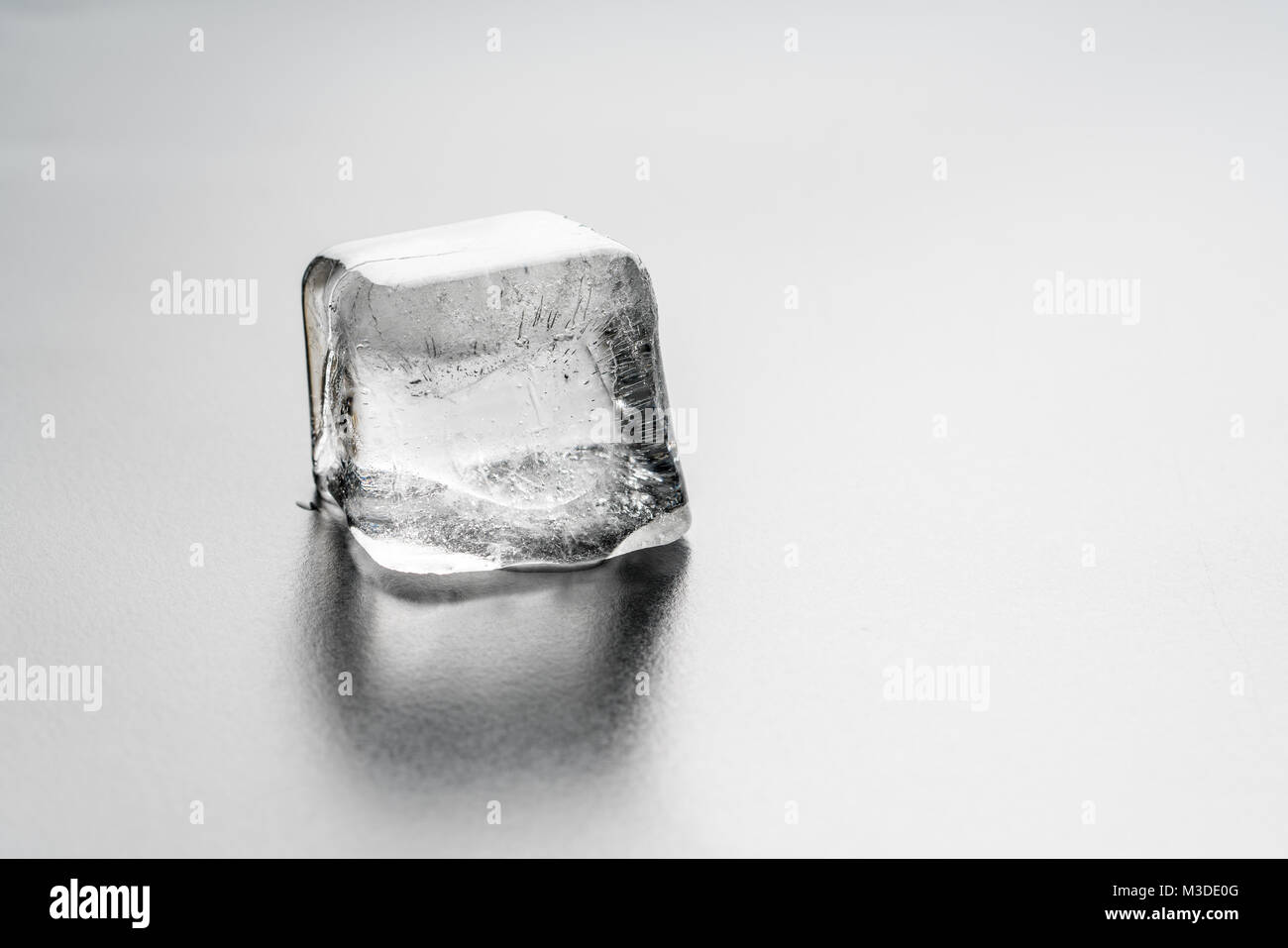 Close up of a single square ice cube on a plain slightly reflective ...