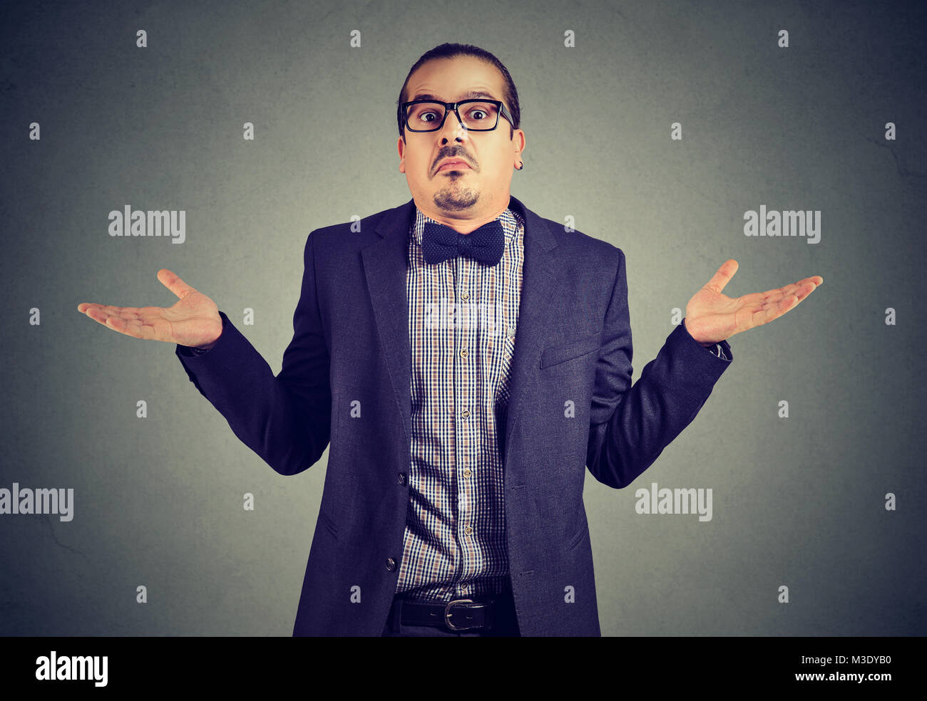 Young man in formal clothing shrugging shoulders while posing on gray ...