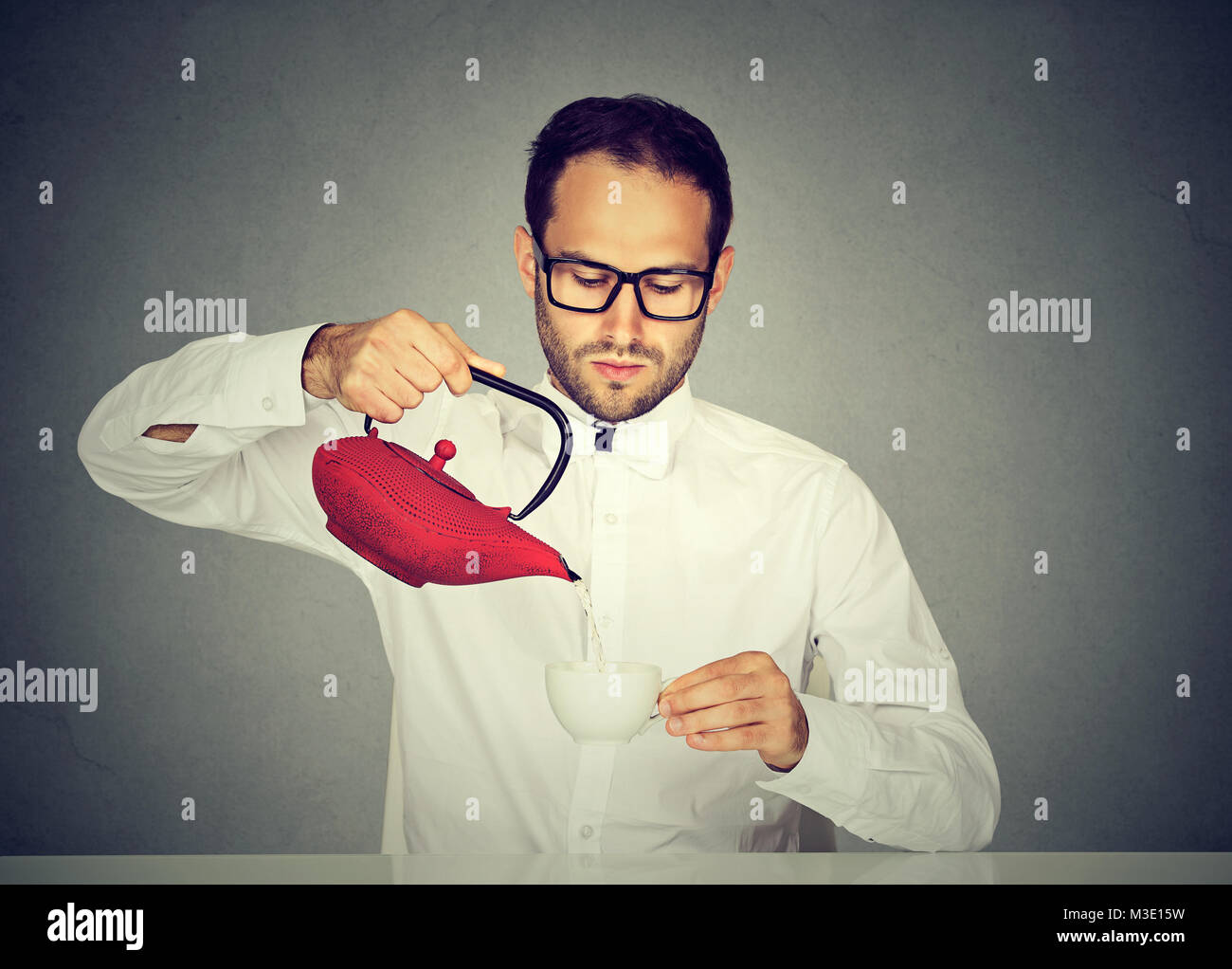 Young elegant gentleman pouring tea in cup looking serious while having ...