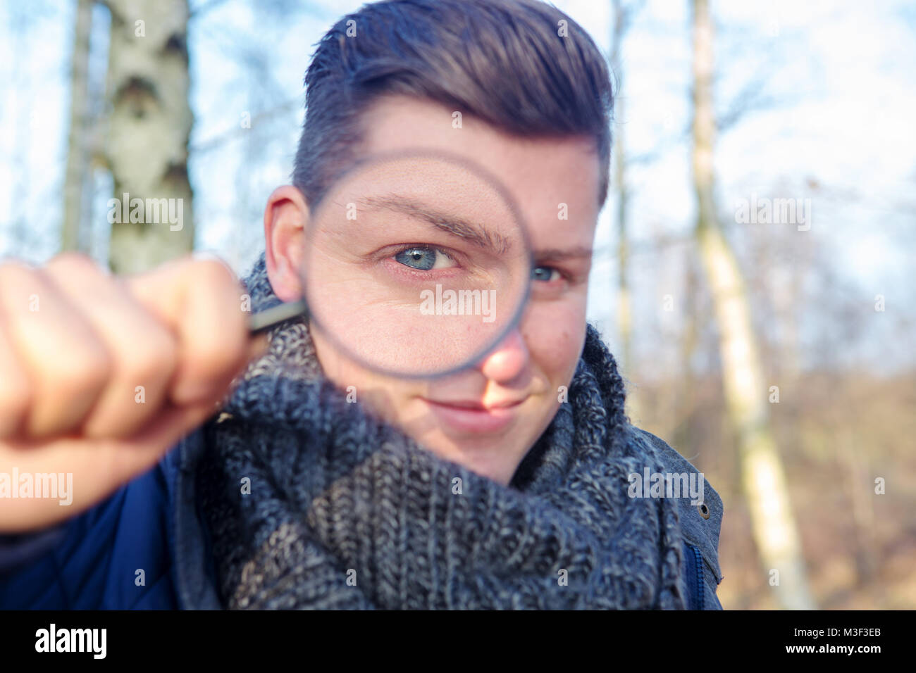 portrait of handsome man looking through a magnifying glass outdoors ...