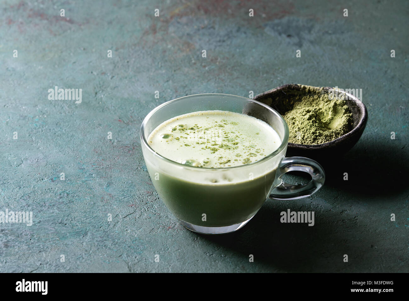 Cup of matcha latte with bowl of matcha tea over grey green texture ...