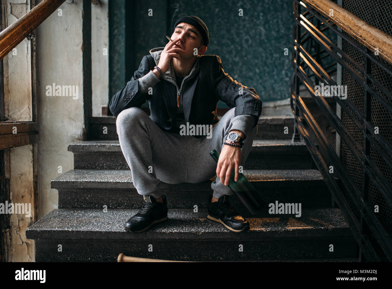 Bad guy with bottle of beer sits on the stairs and smoking. Street ...