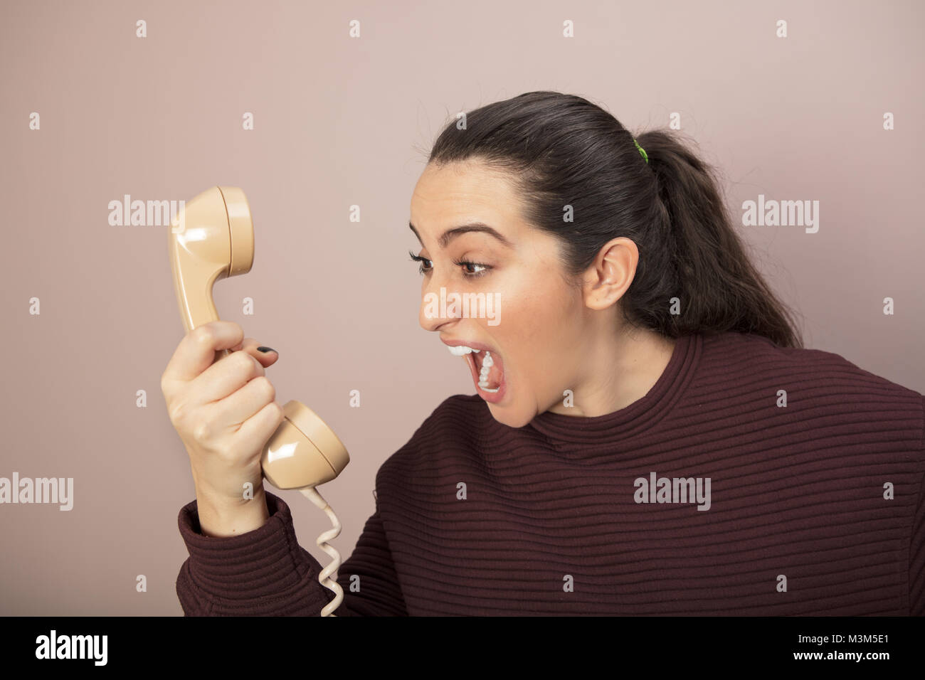 Frustrated angry woman screaming at the telephone as she grips a corded ...