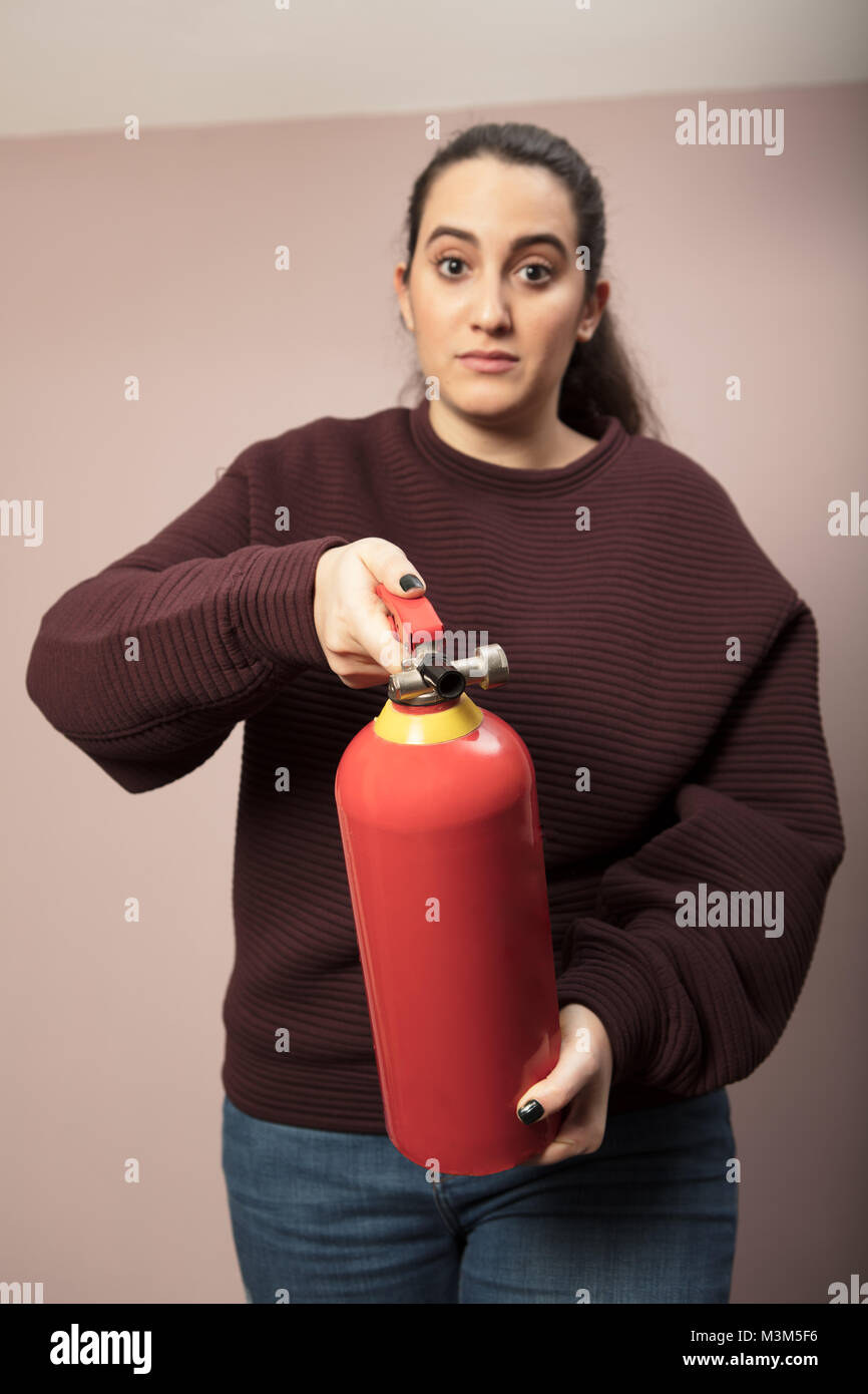 Young woman pointing a red fire extinguisher forwards towards the ...