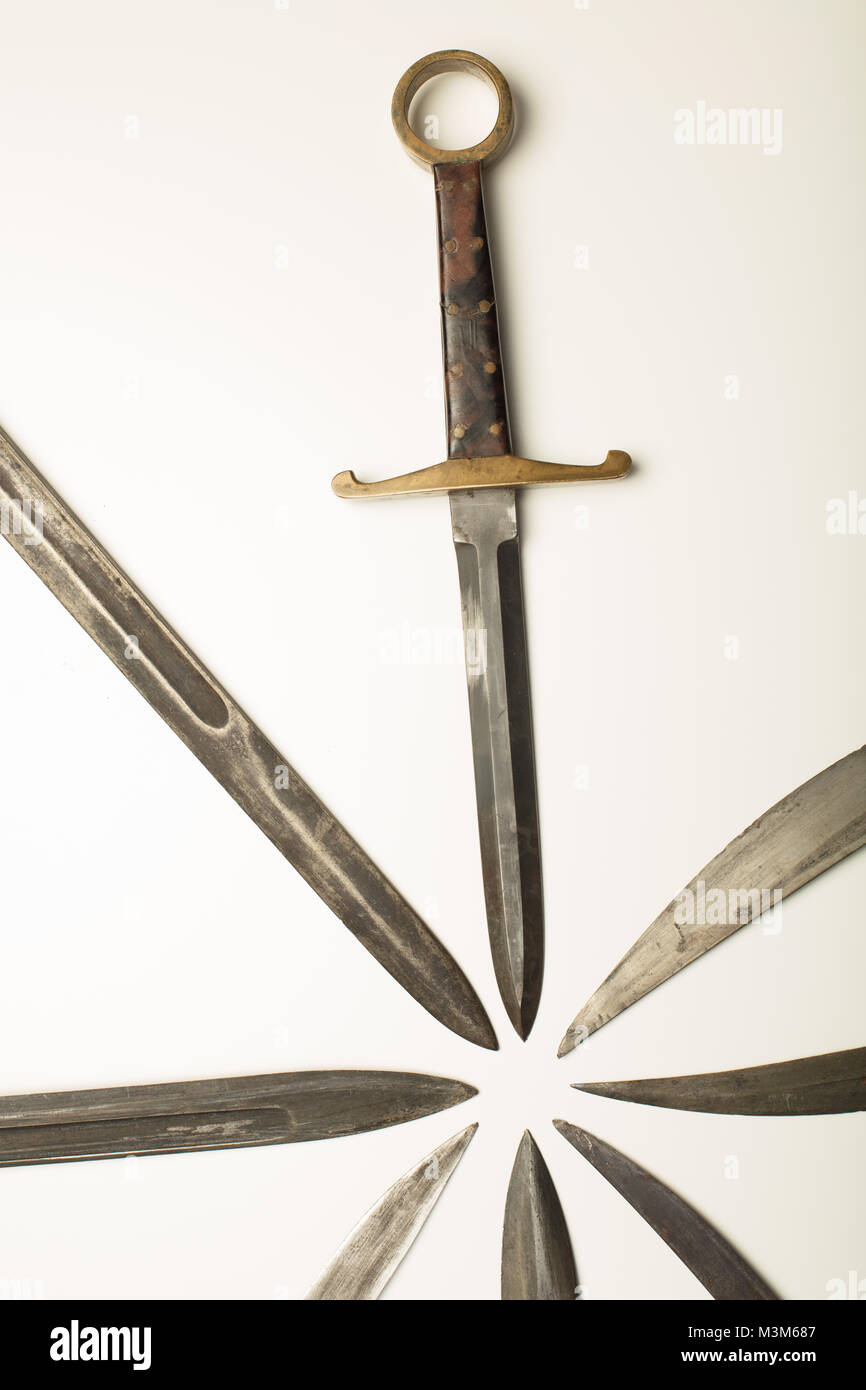 Isolated old dagger with assorted blades of weapons all pointing to a ...