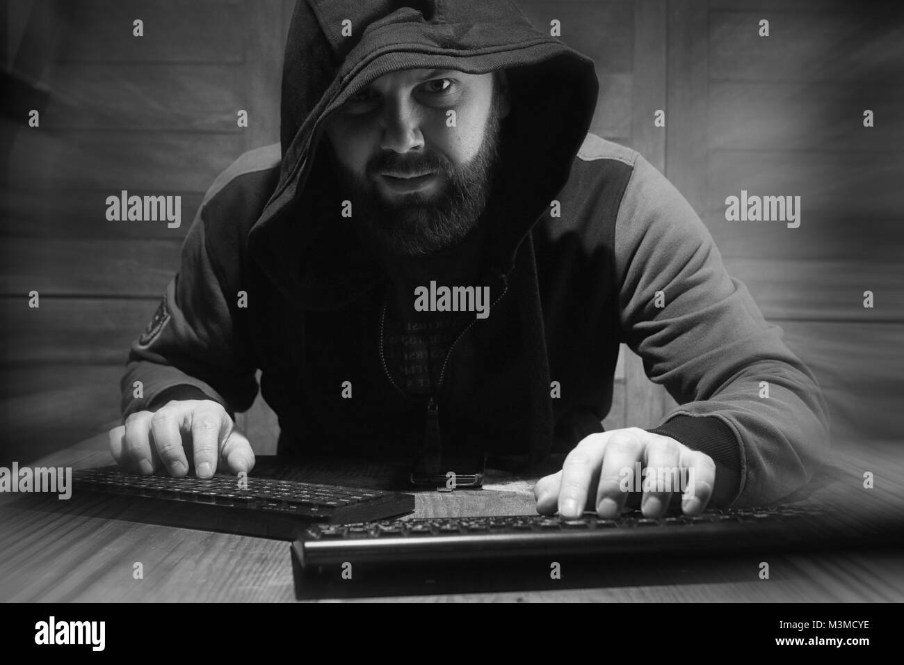 The hacker in the hood sits and works behind the computer Stock Photo ...