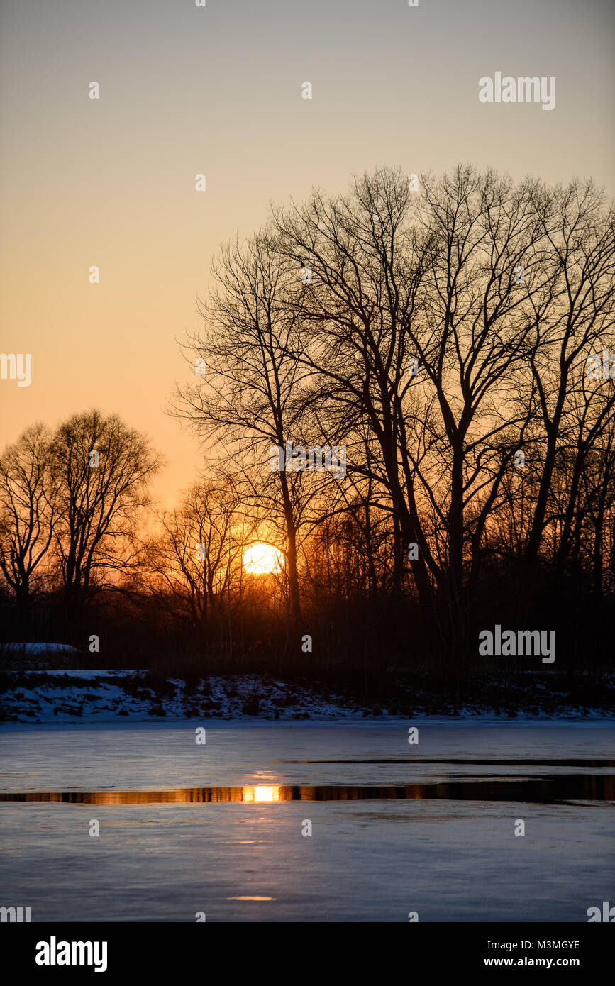 colorful winter sunset with trees and power lines in background and ice ...