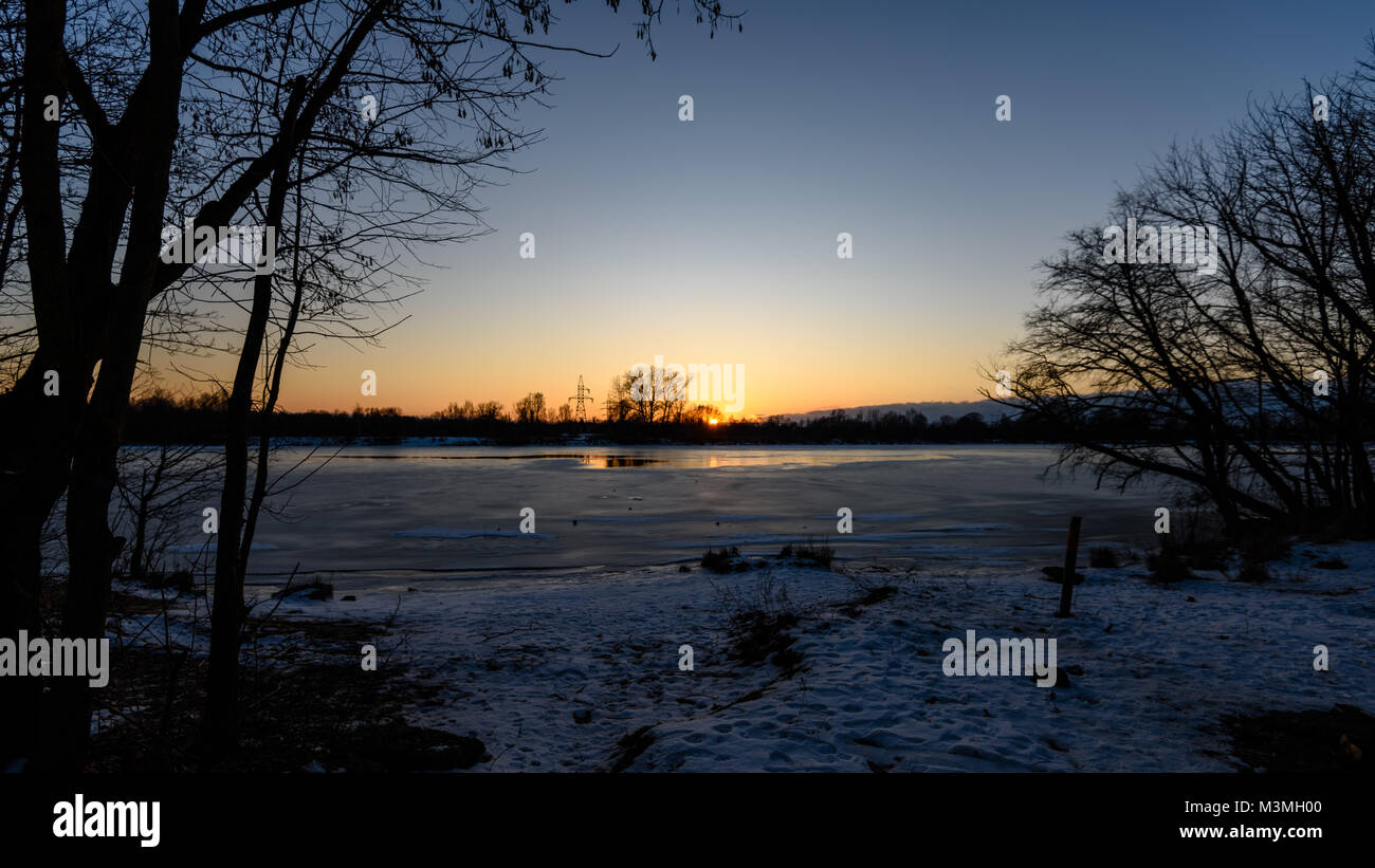 colorful winter sunset with light rays coming through the trees on the ...