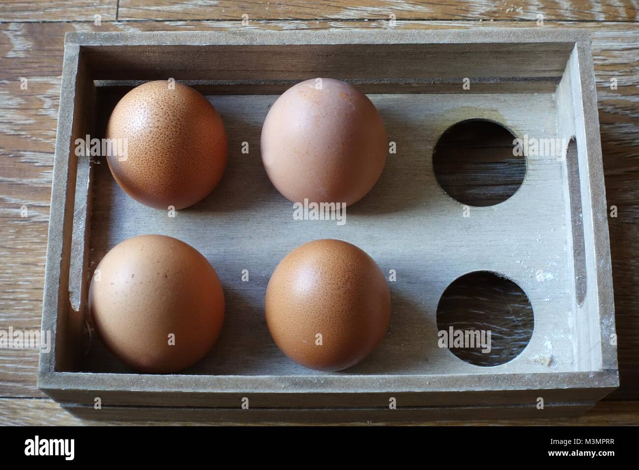 Four brown eggs in a wooden box with space for six eggs, in window ...