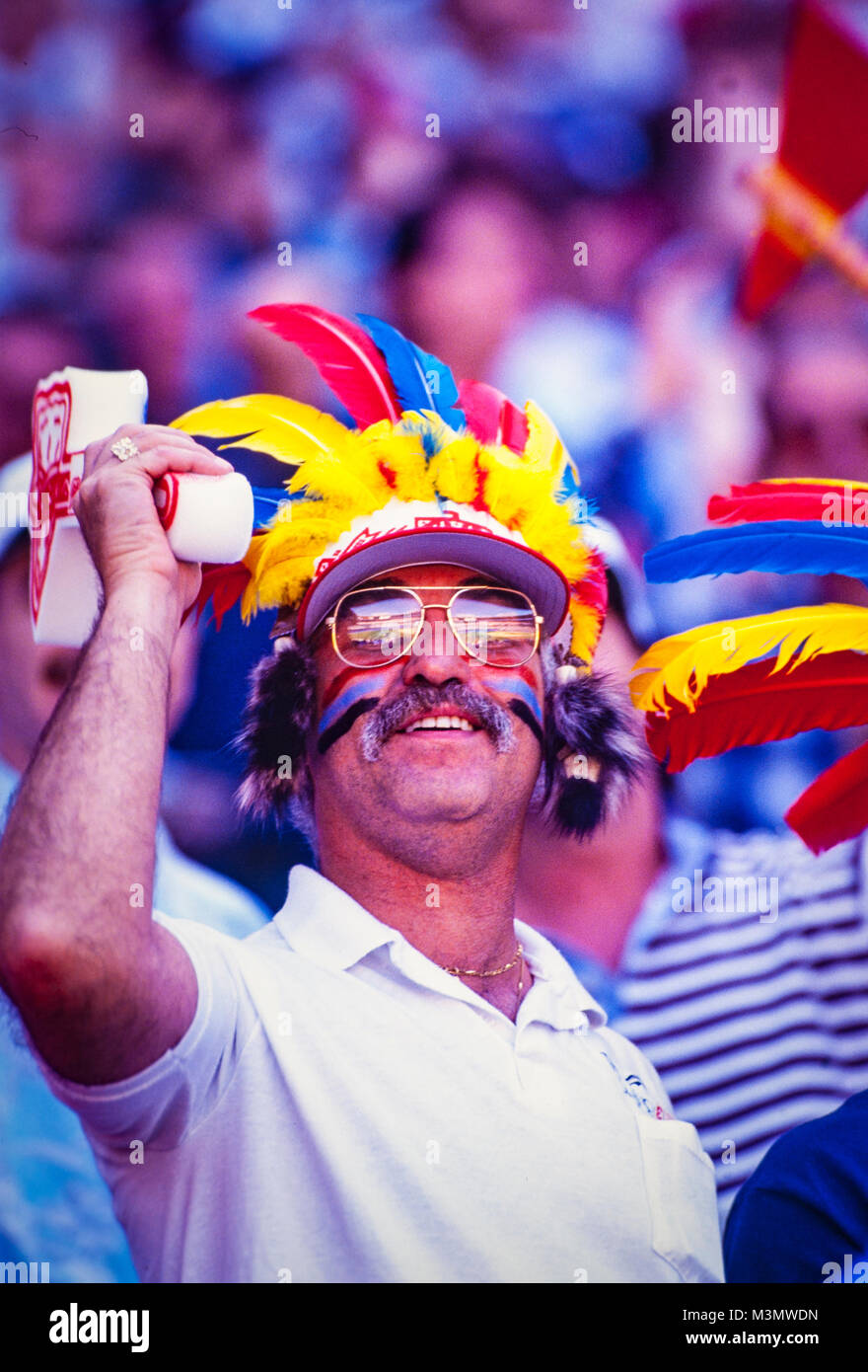 A baseball fan wearing a headdress with feathers swings a foam tomahawk ...