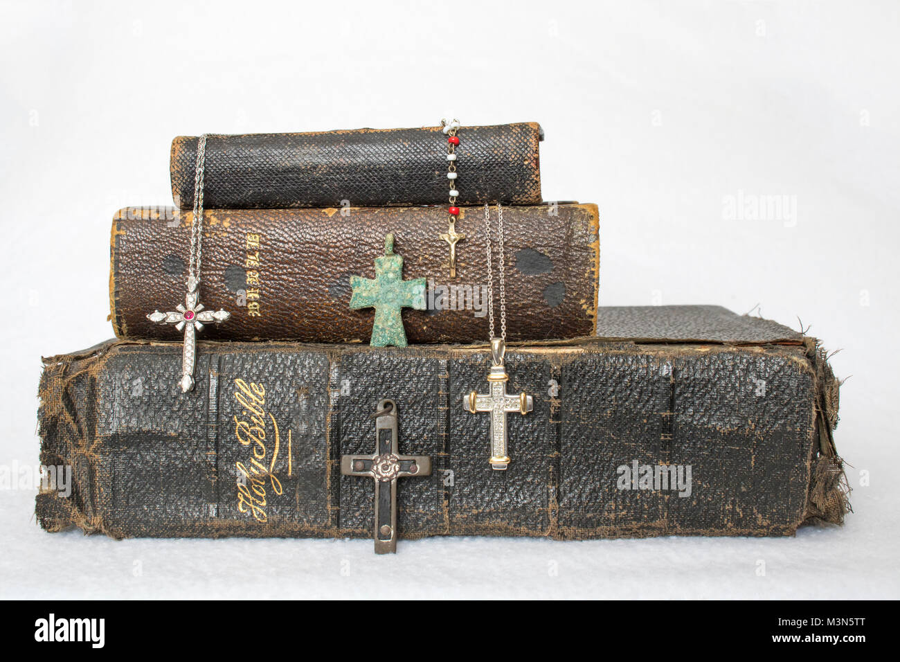 Stack of Antique Leather Bibles with Five Crosses from Ancient Bronze to Modern Diamond on White ...