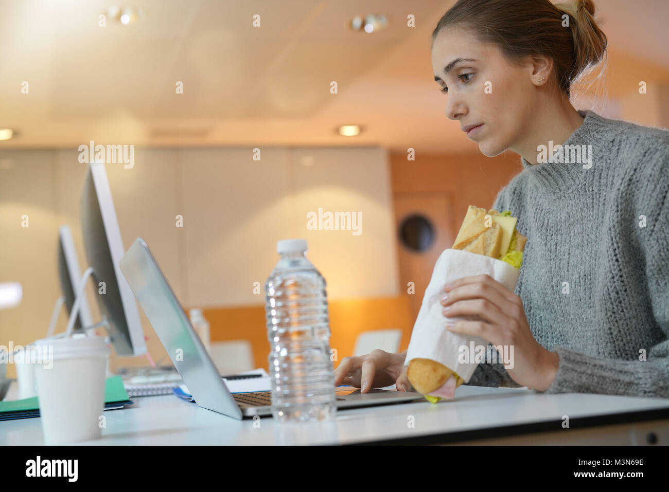 Young woman student eating sandwich in front of laptop computer Stock ...