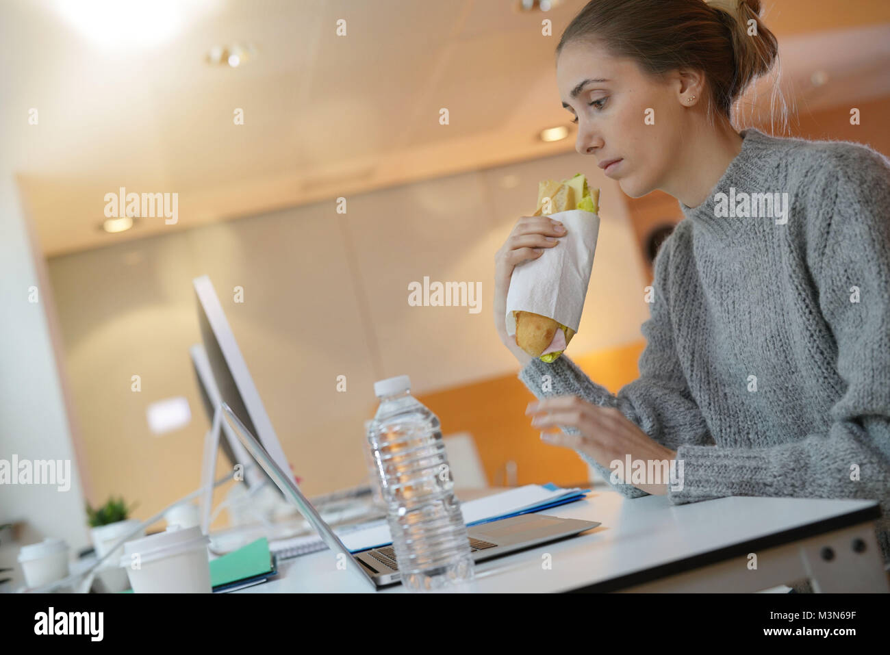 Young woman student eating sandwich in front of laptop computer Stock ...