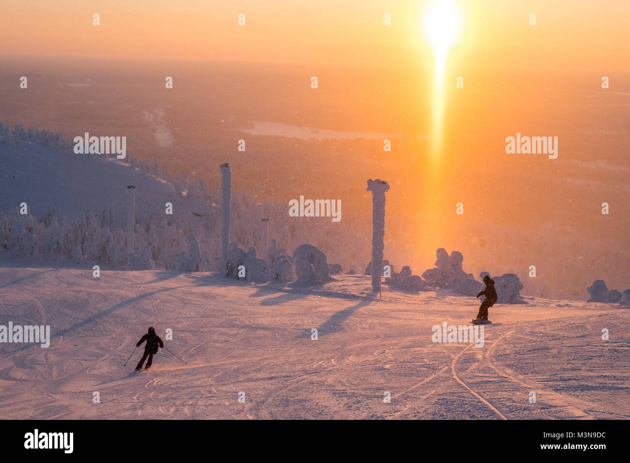Skier and snowboarder on a piste in Ruka Finland with a low setting sun ...