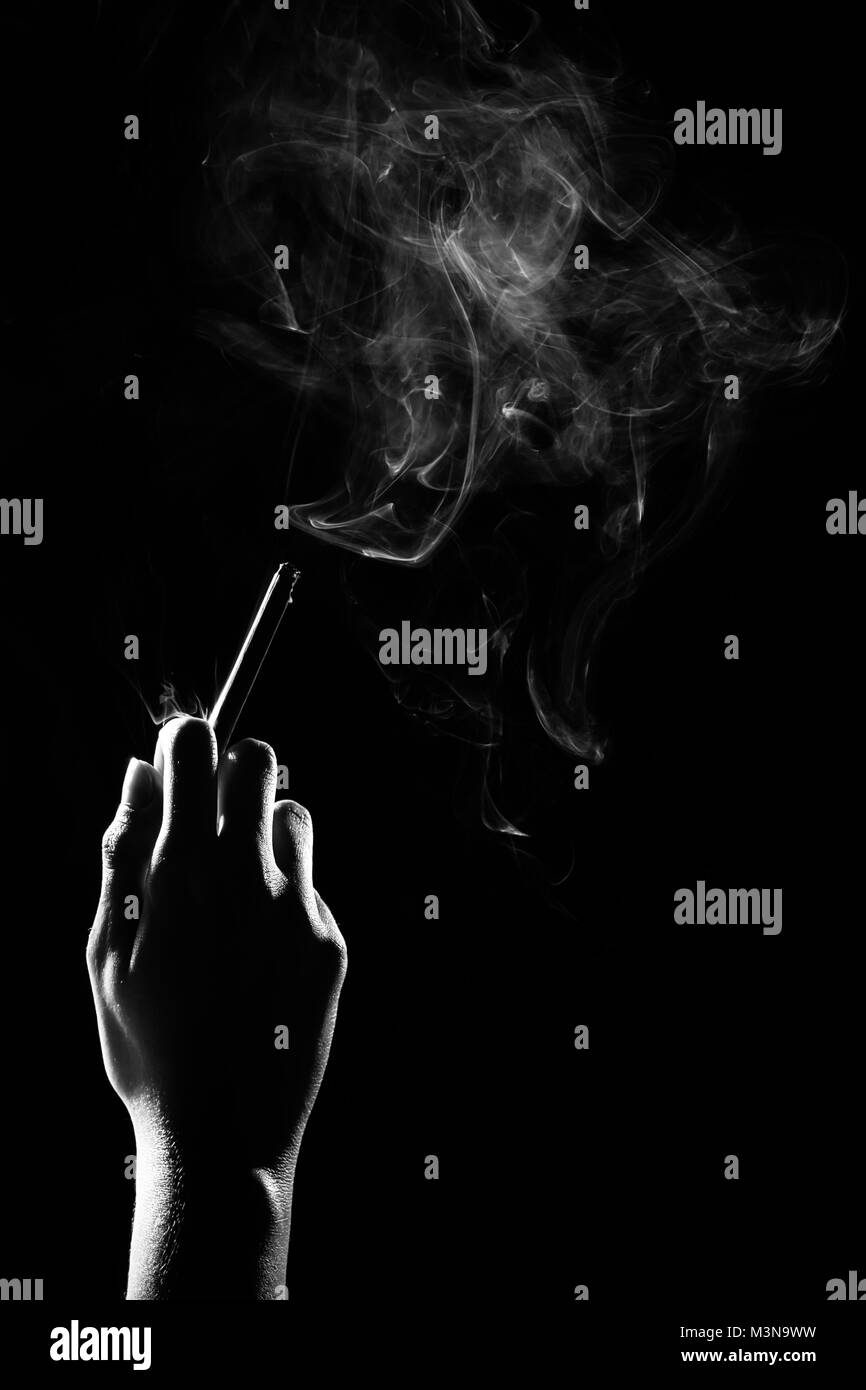 hand with burning cigarette and smoke on black background, monochrome ...