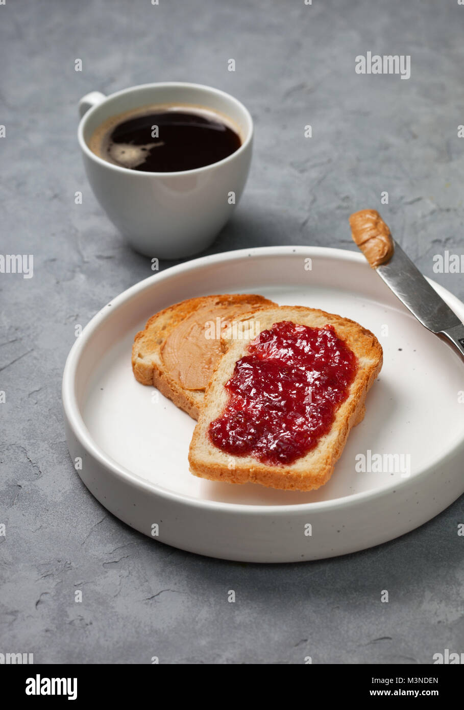 two toasts with peanut butter and jam, a cup of coffee on a gray ...