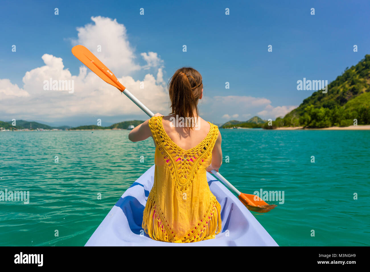Rear view of a young woman paddling a canoe on the sea in a sunny day ...