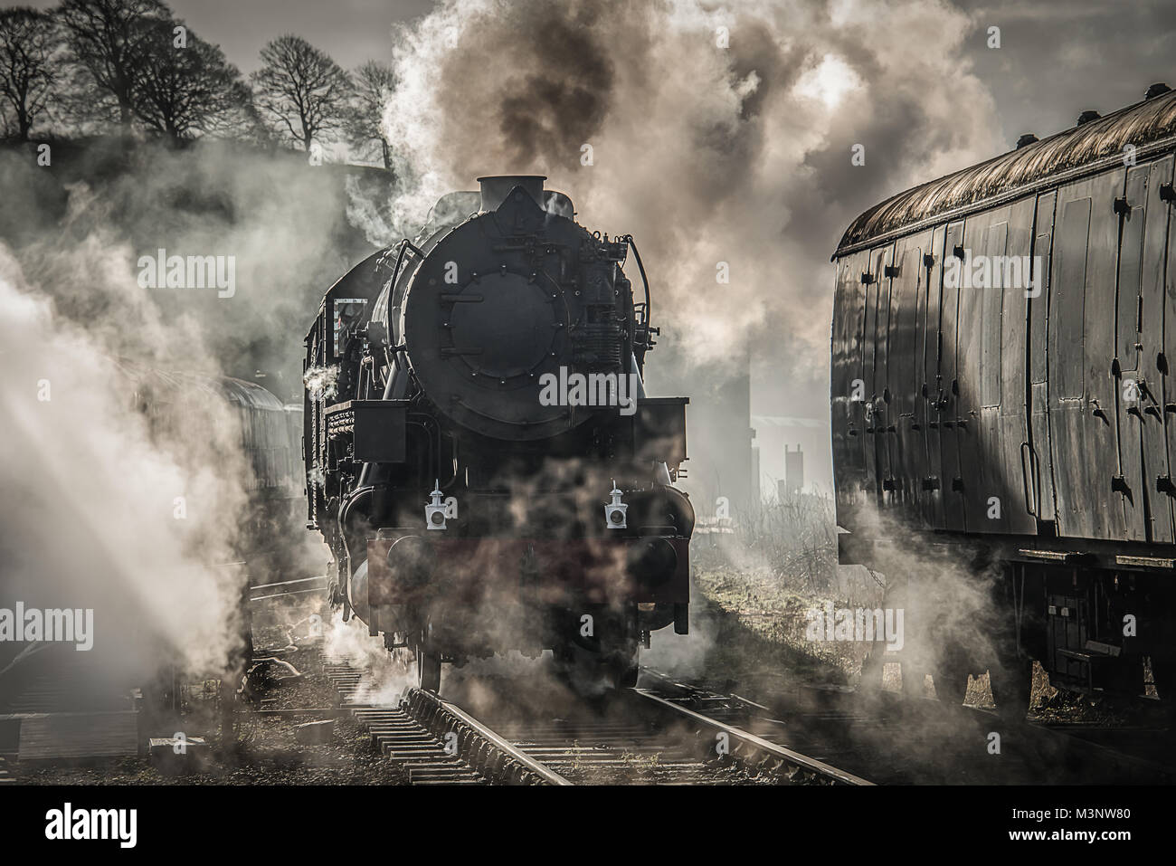 A early morning back lit photograph of a steam train smoking and ...