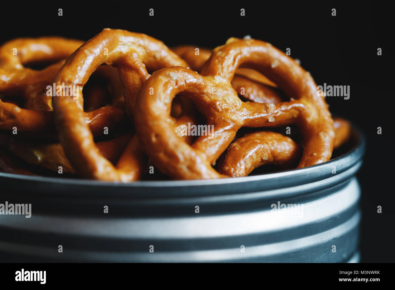 Crunchy pretzels appetizer in a metal jar against black background ...