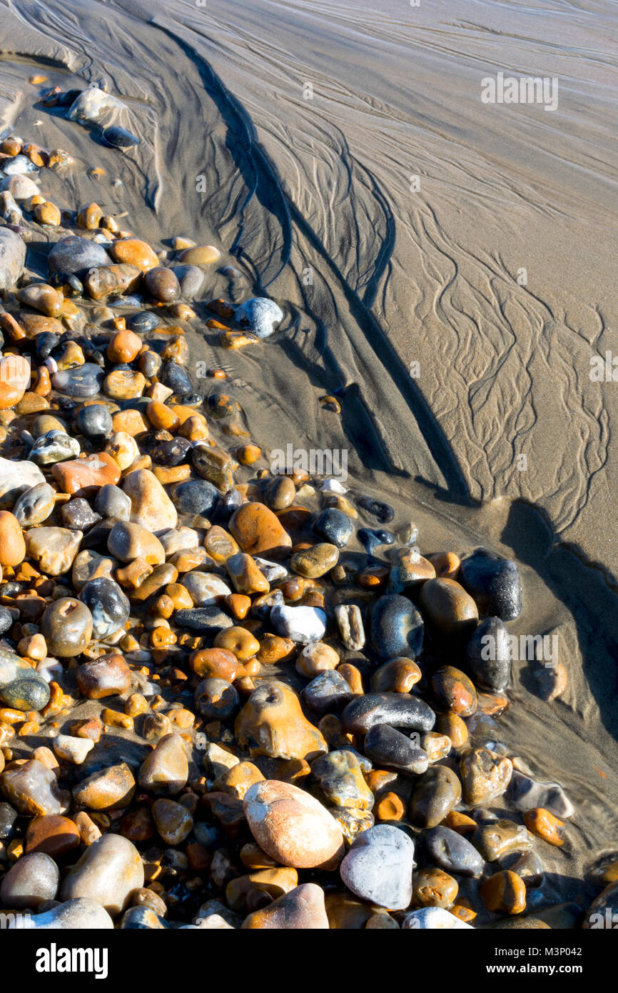 Shingle and pebbles next to wet sand in sunshine Stock Photo - Alamy