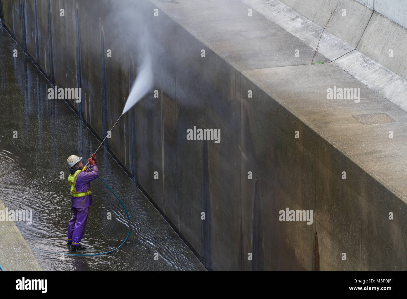 A workman uses high pressure water hose to jet clean a storm drain ...