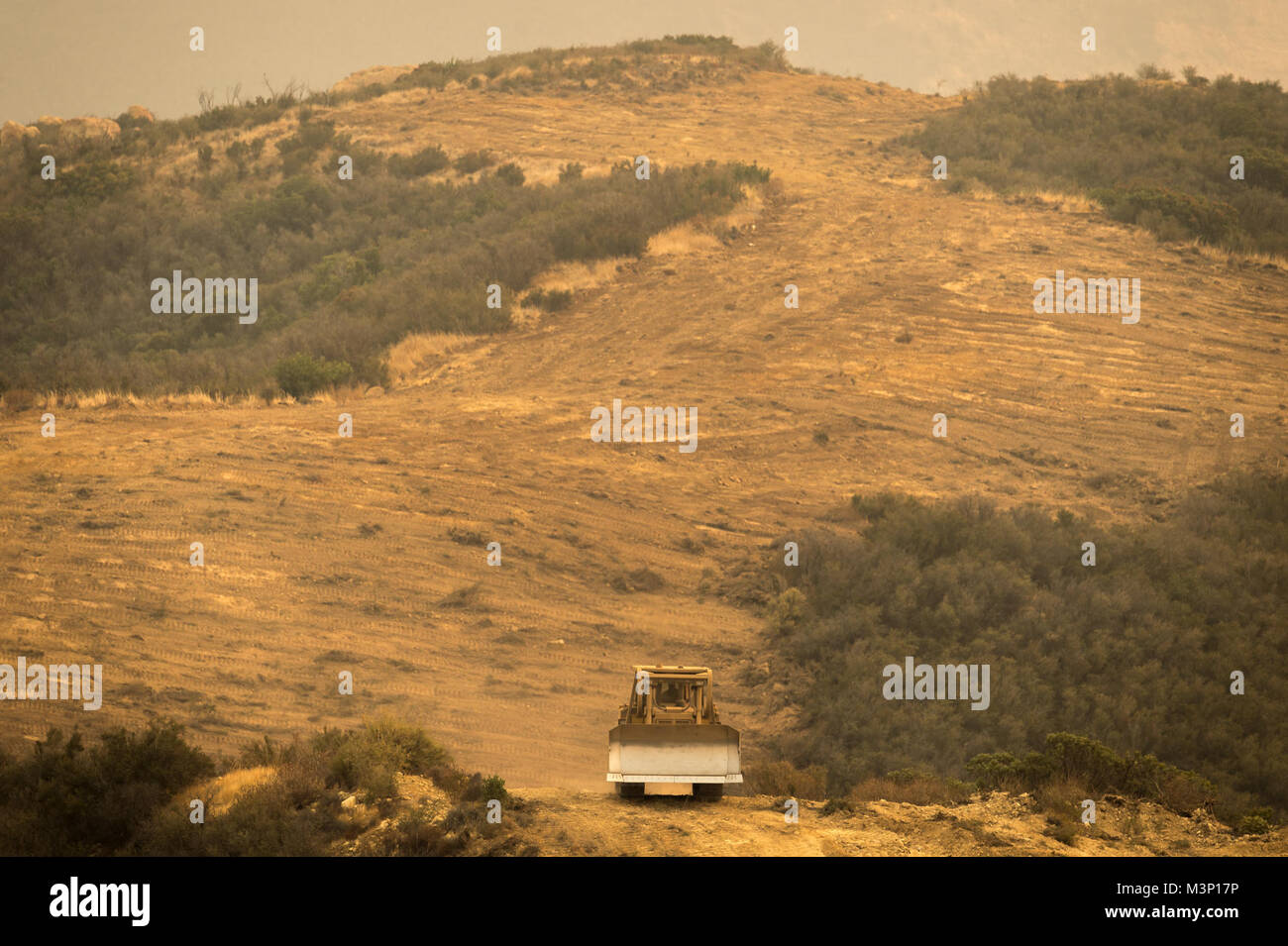 A bulldozer clears away foliage to form a fire-break on a ridge in the ...