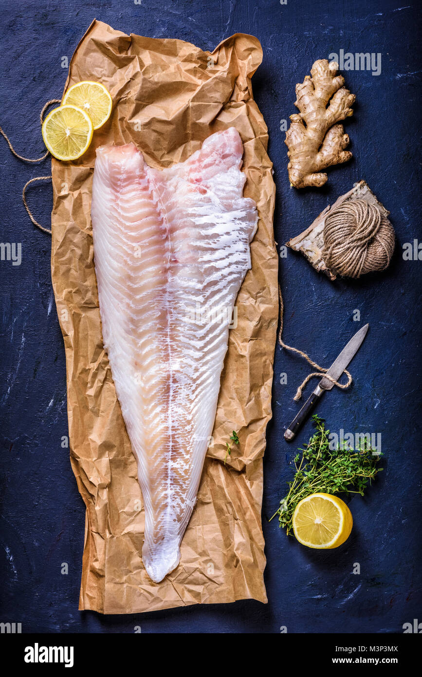 top view of raw fish fillet with lemon, ginger, rope and knife on blue ...