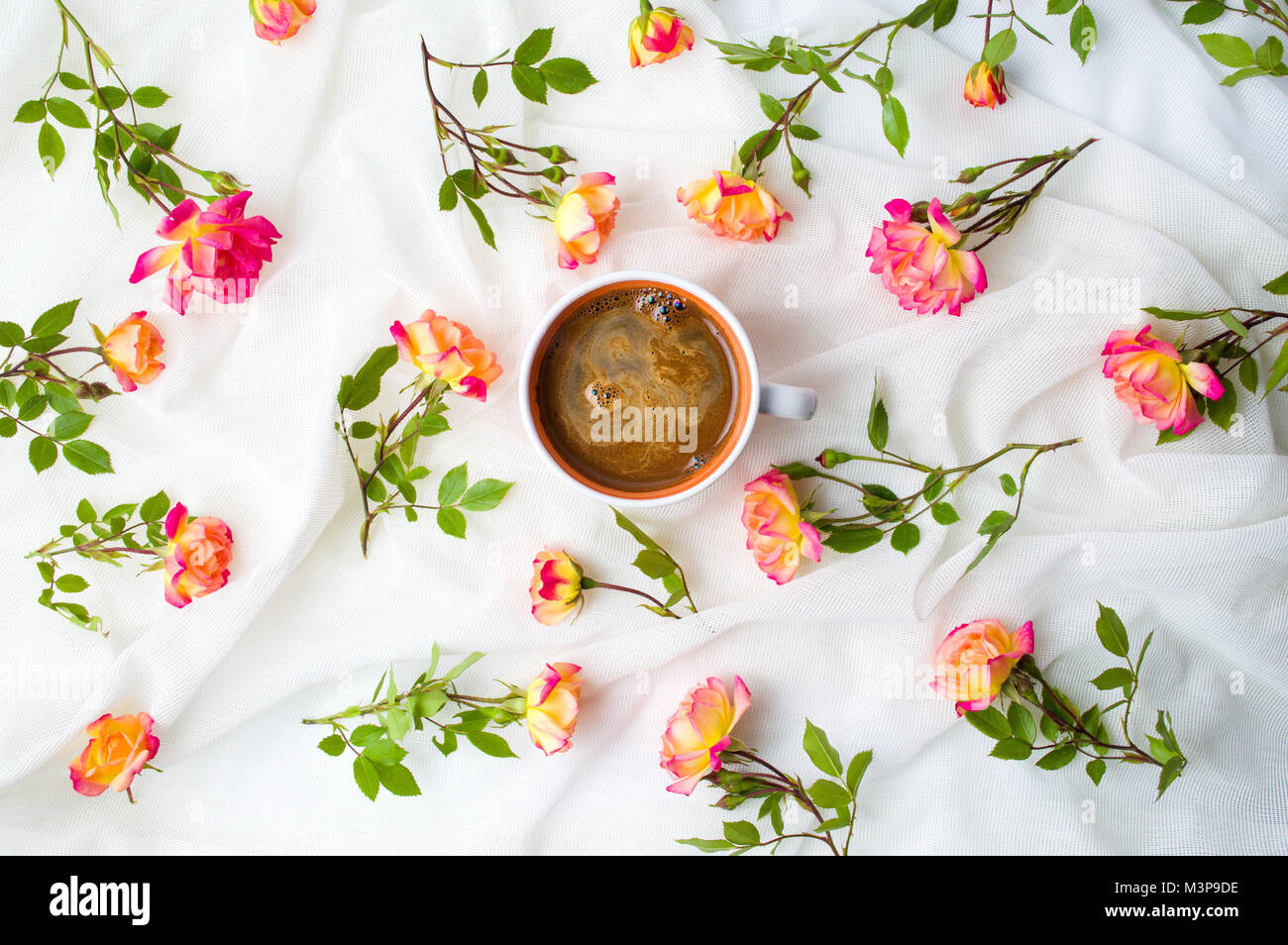 Orange roses and a cup of coffee on white fabric flatlay Stock Photo ...