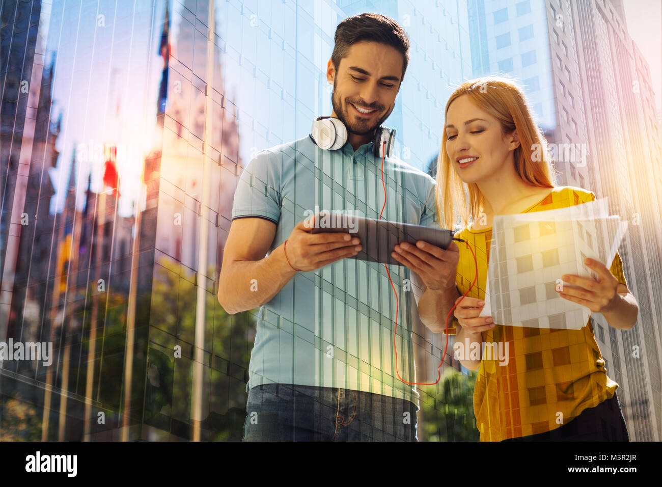 Young man smiling while showing his tablet to a friendly fellow student ...