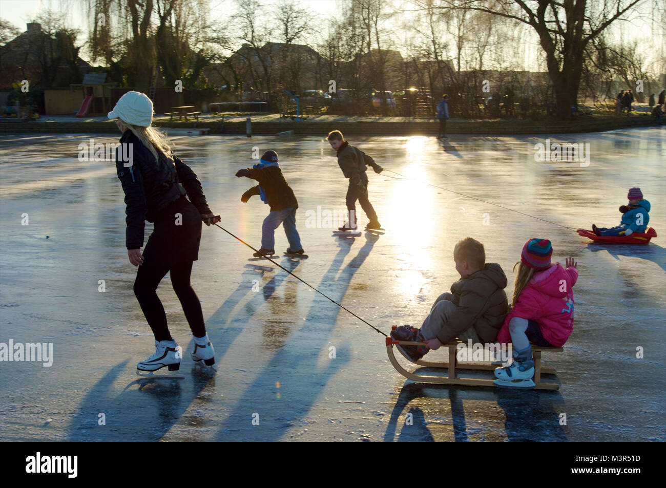 Young mother with children pulling a sled and skating on ice together ...