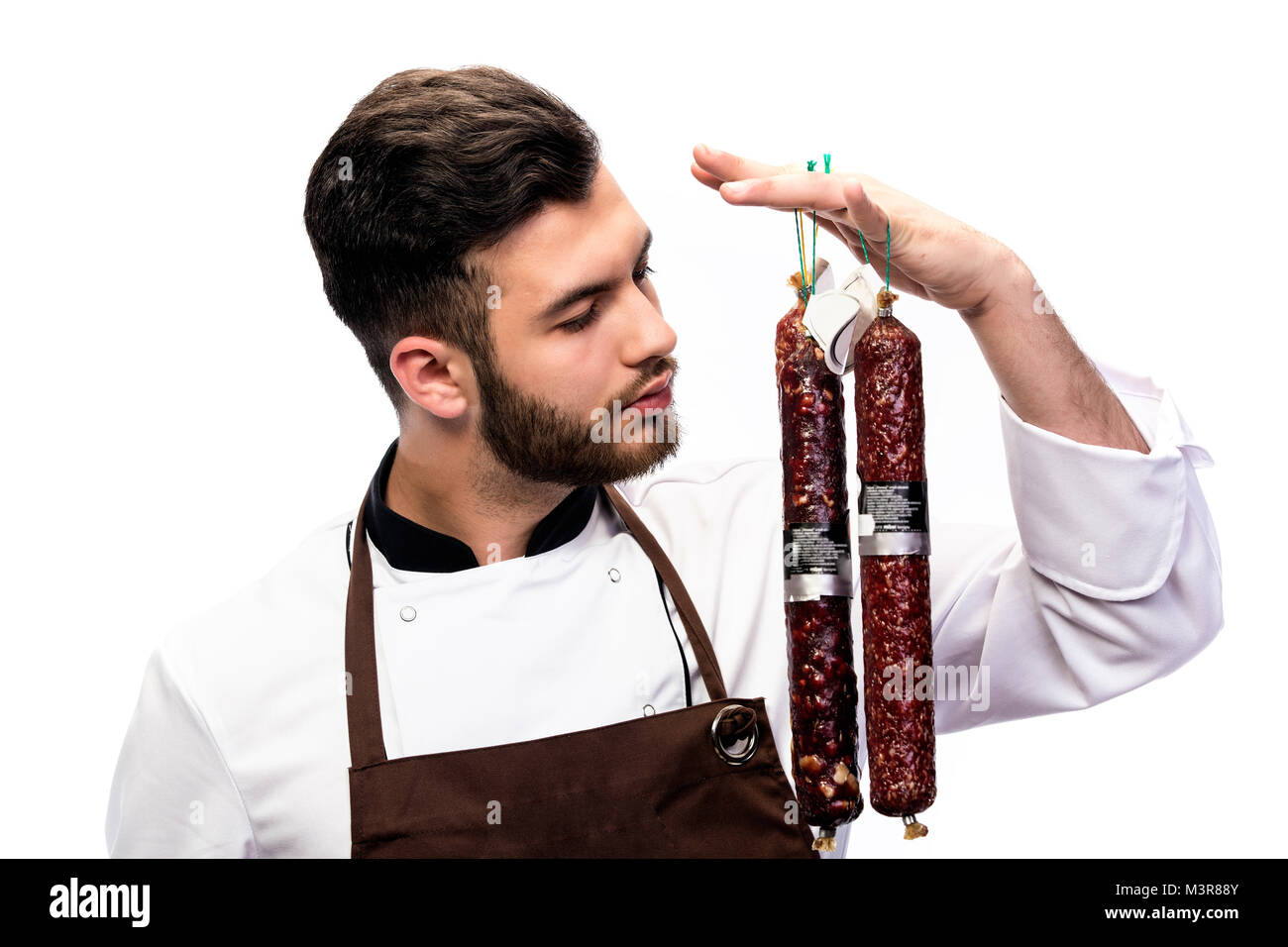 portrait of a young man in a chef's apron. Cook sniffing salami on ... portrait of a young man in a chef's apron. Cook sniffing salami on ...