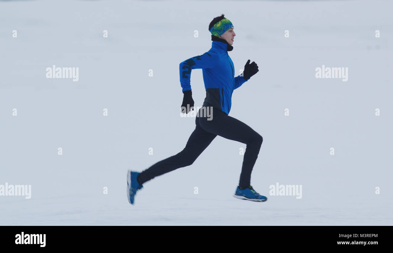 Young male athlete running fast in winter through the snowy ice field ...