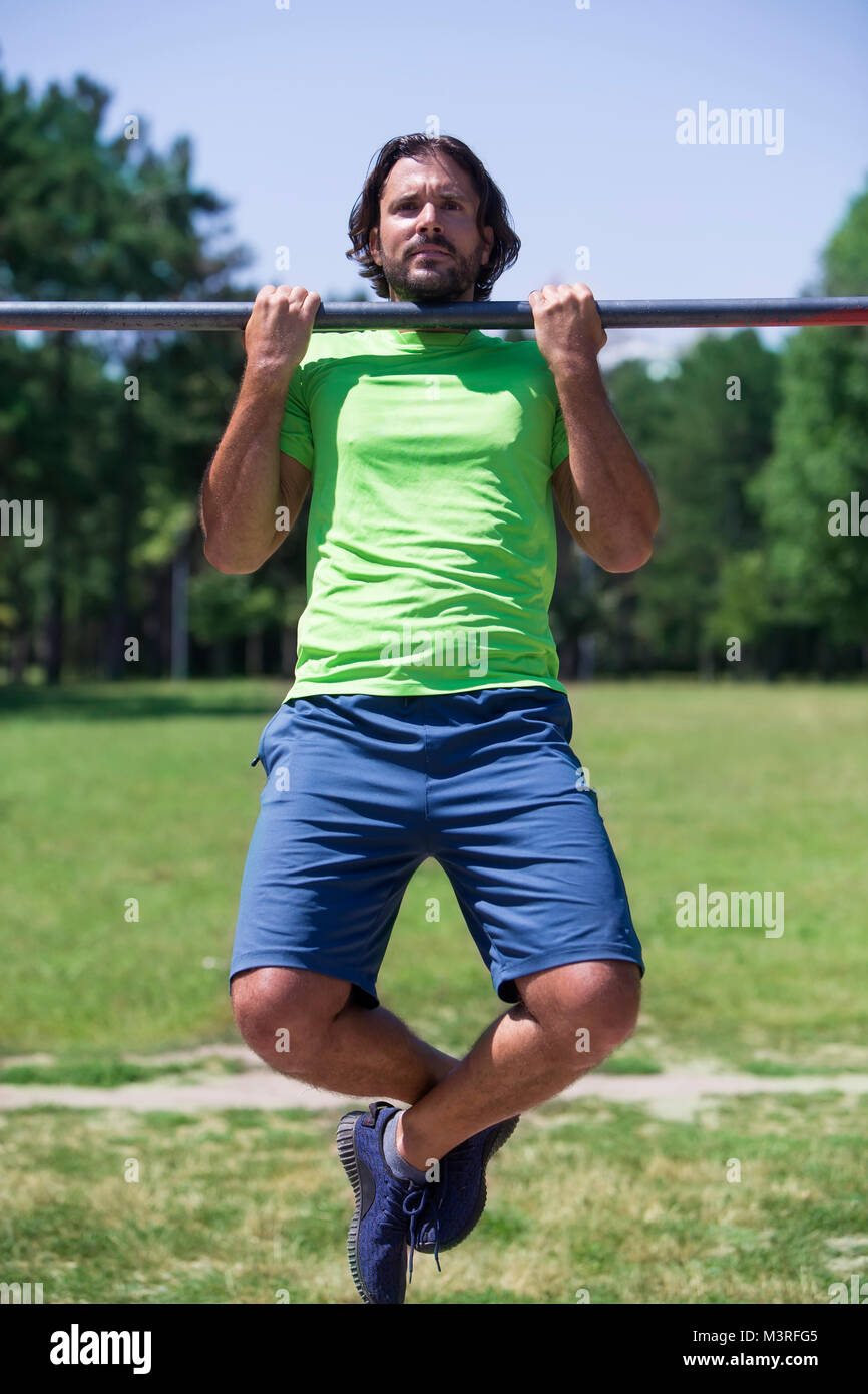 Muscular man doing pull-ups on horizontal bar in park Stock Photo - Alamy