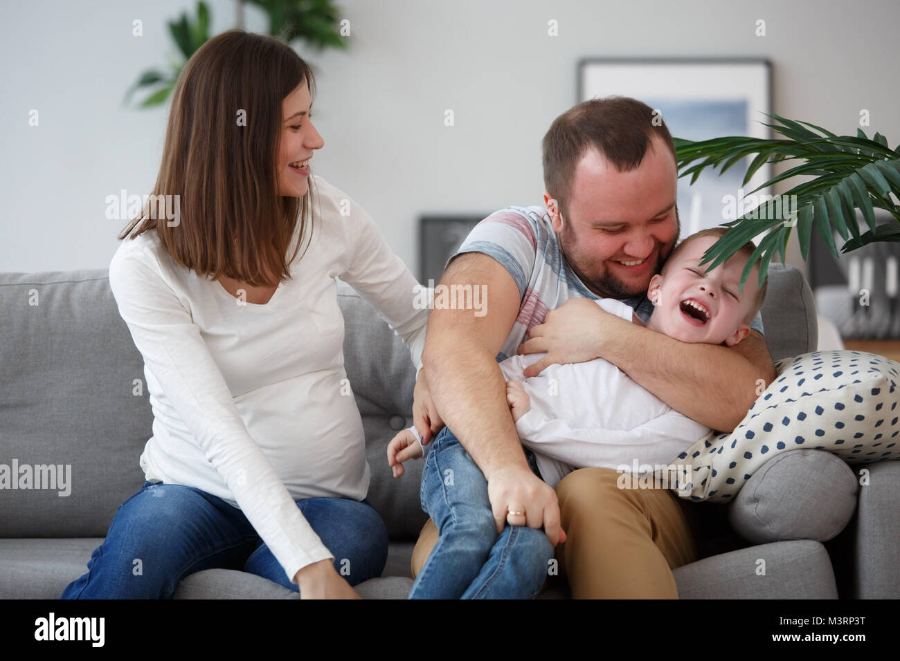 Picture of smiling parents with son sitting on gray sofa Stock Photo ...