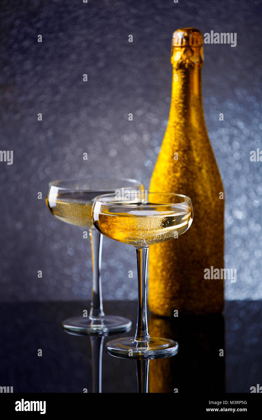 Image of bottle of sparkling wine in gold wrapper with two wine glasses ...