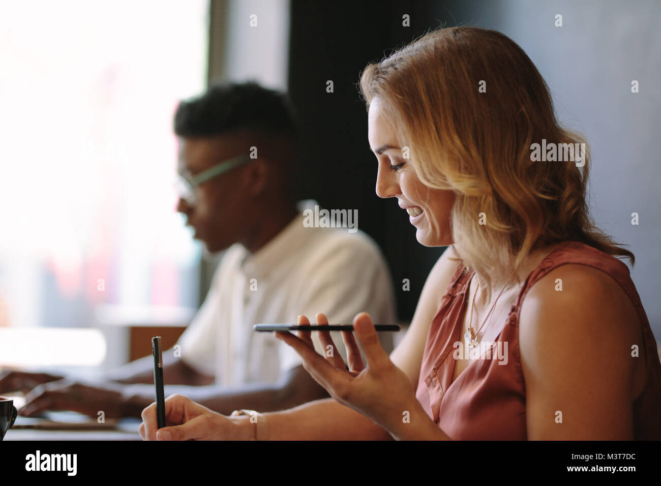 Woman entrepreneur writing in notepad while talking over mobile phone ...