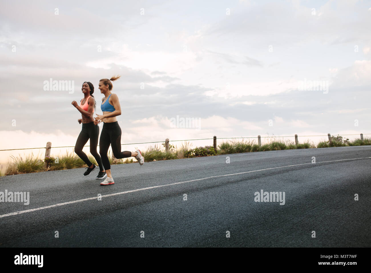 Two women athletes running on road early in the morning with cloudy sky ...