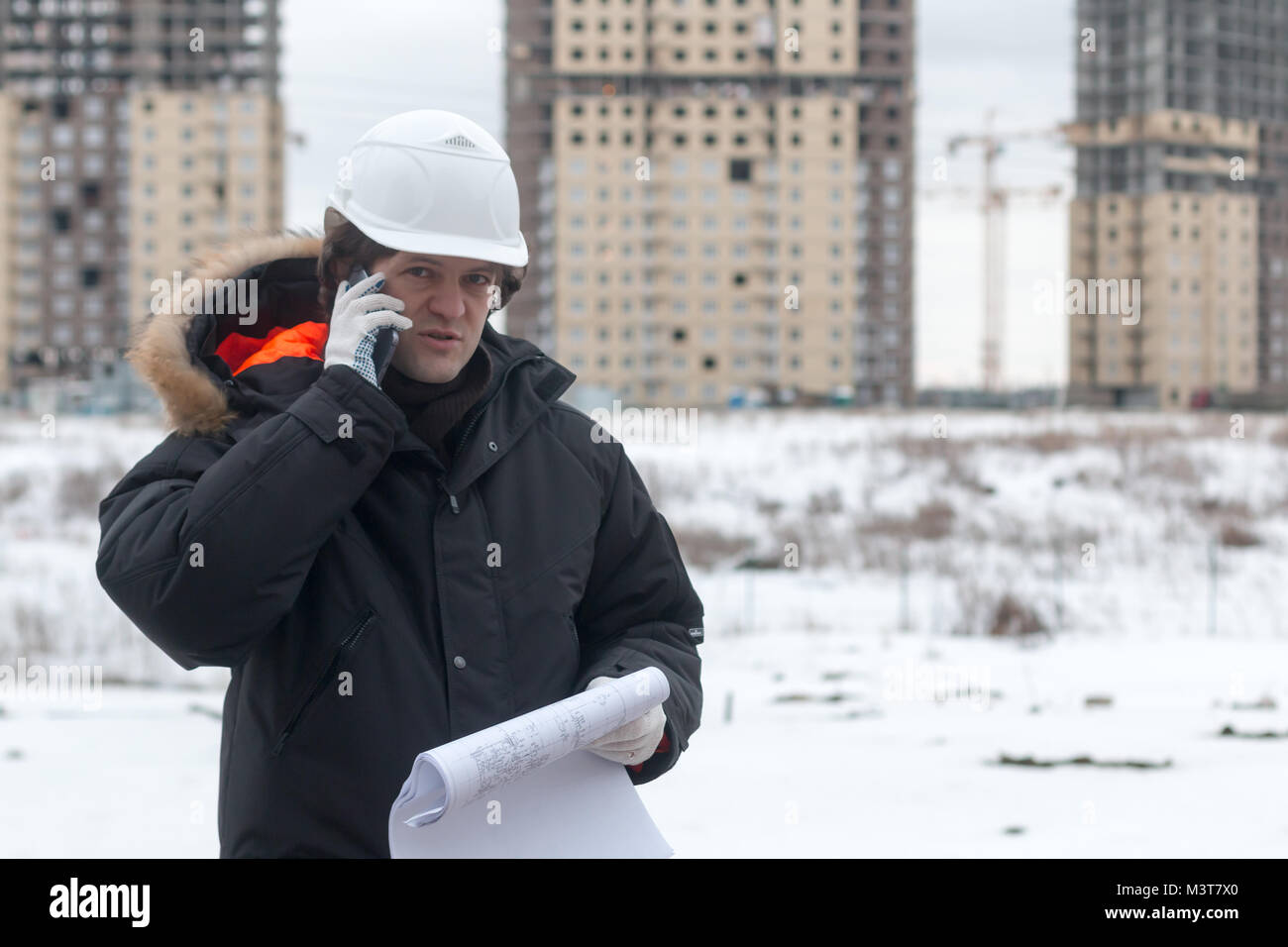 Worker or engineer holding drawing in hands and uses mobile phone on ...