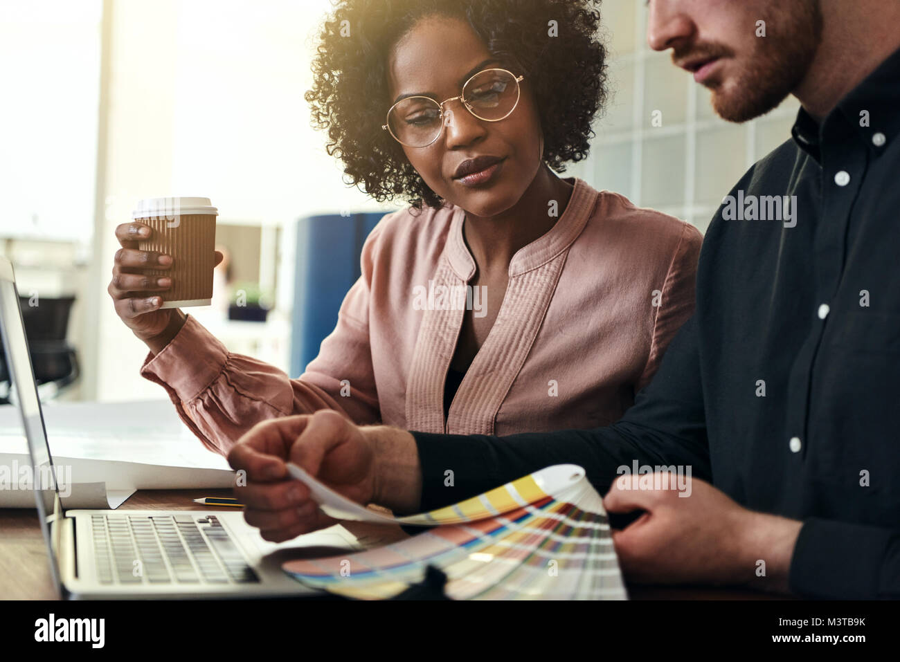 Two designers sitting at a table in a modern office discussing color ...