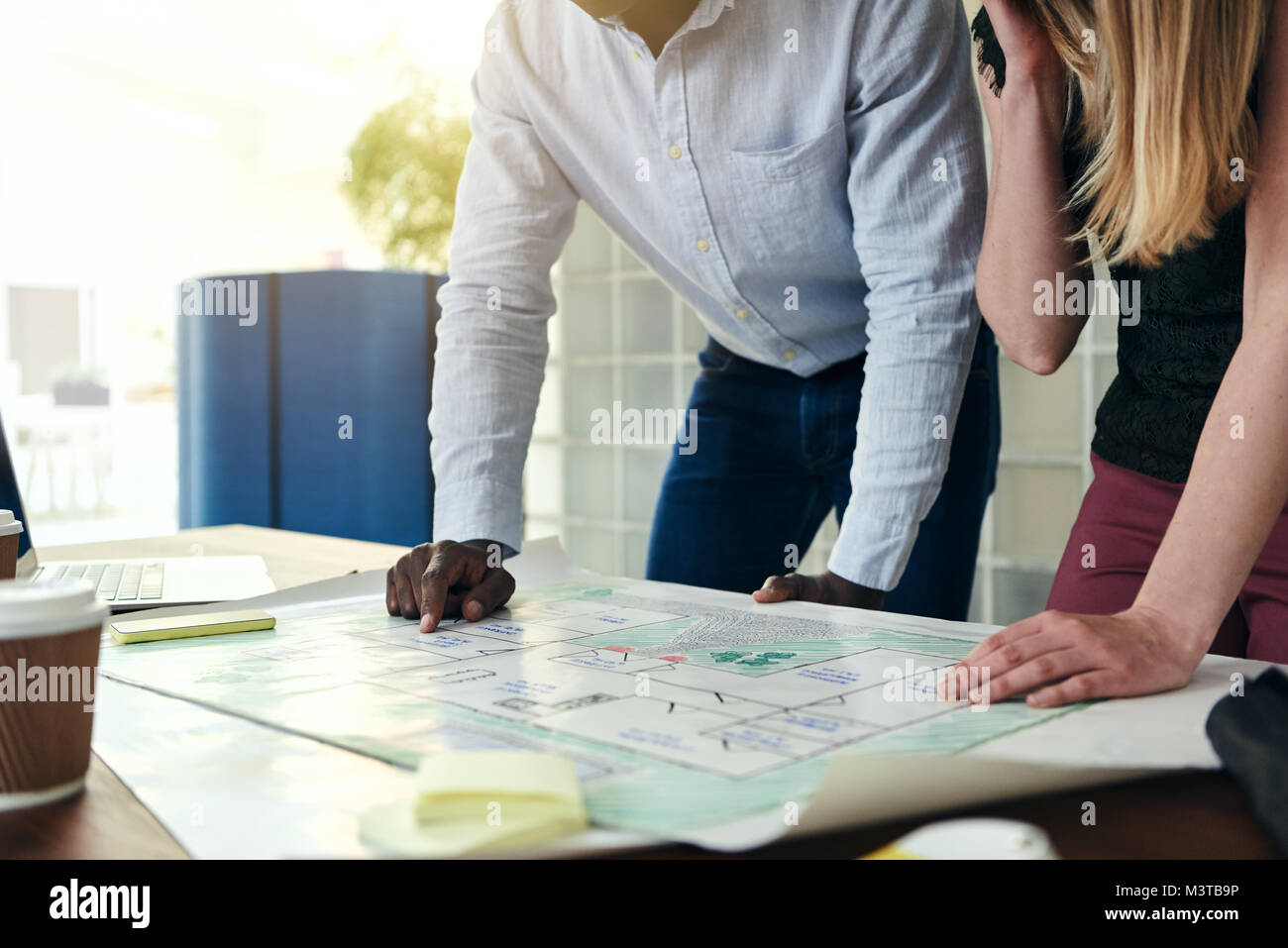 Closeup of two architects standing in a modern office leaning over a ...