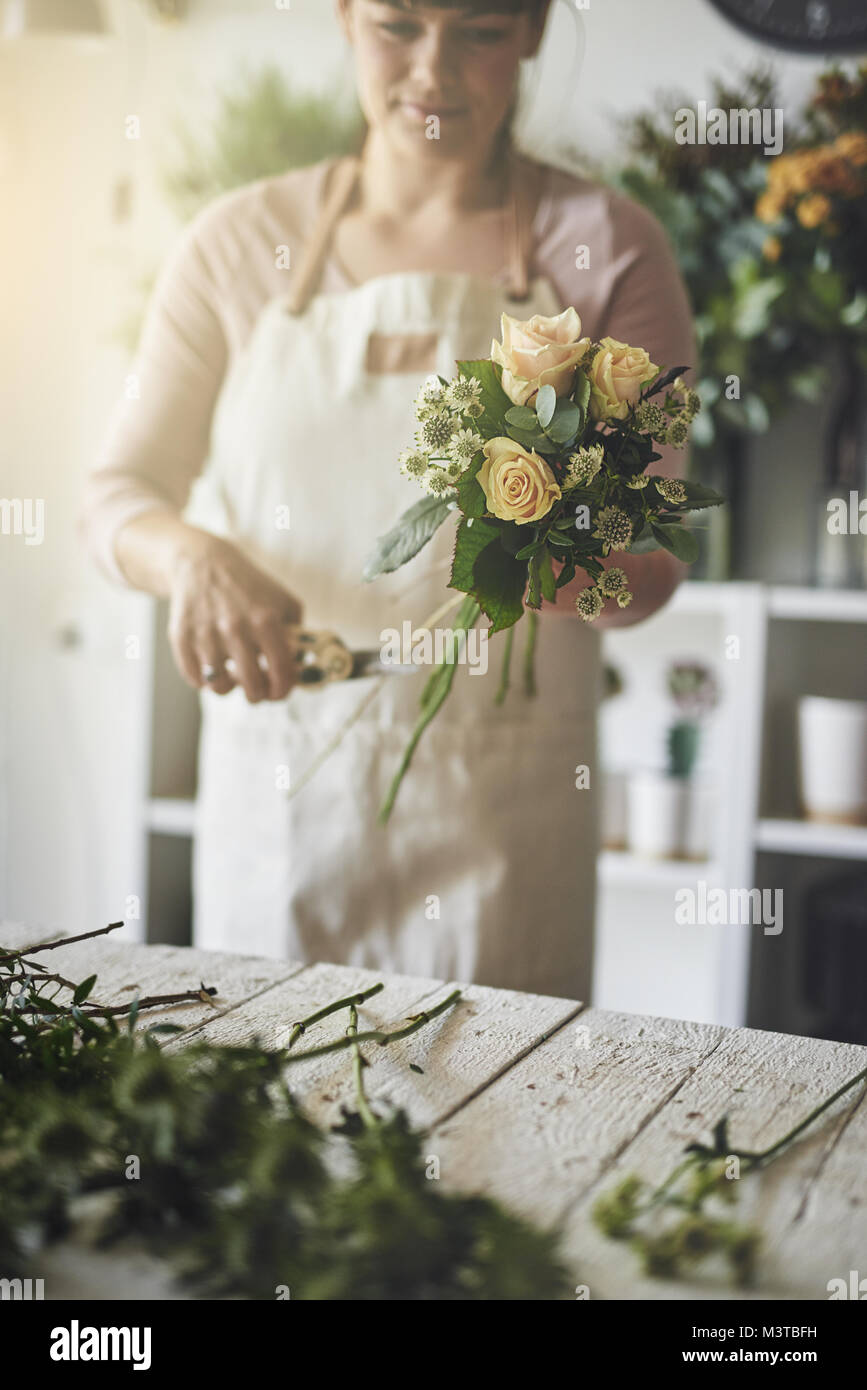 Young female florist trimming the stems of a bouquet of mixed flowers ...