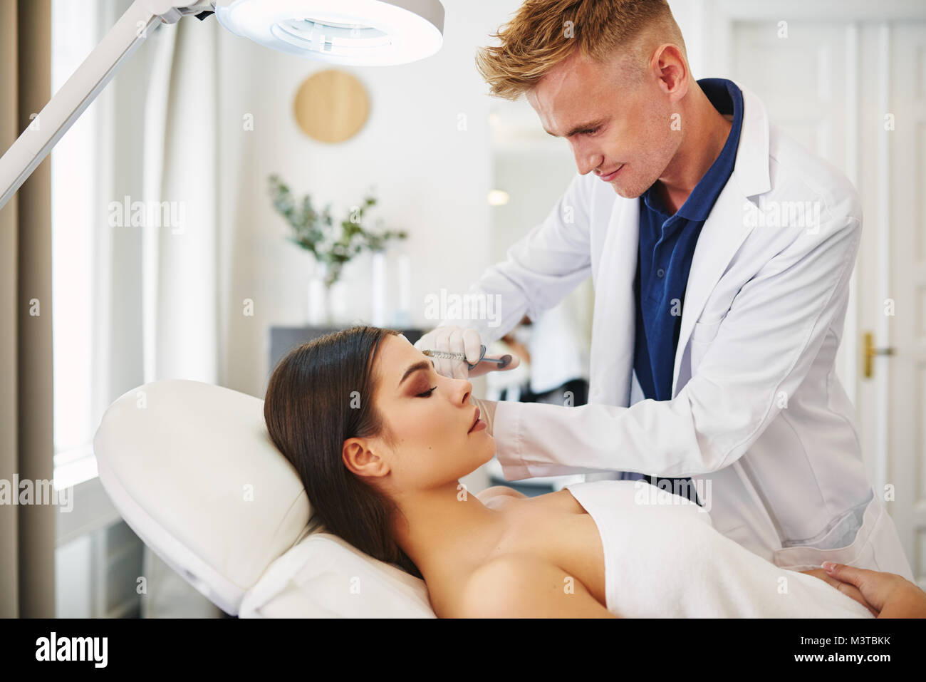 Male doctor performing a botox injection to the face of a young woman ...