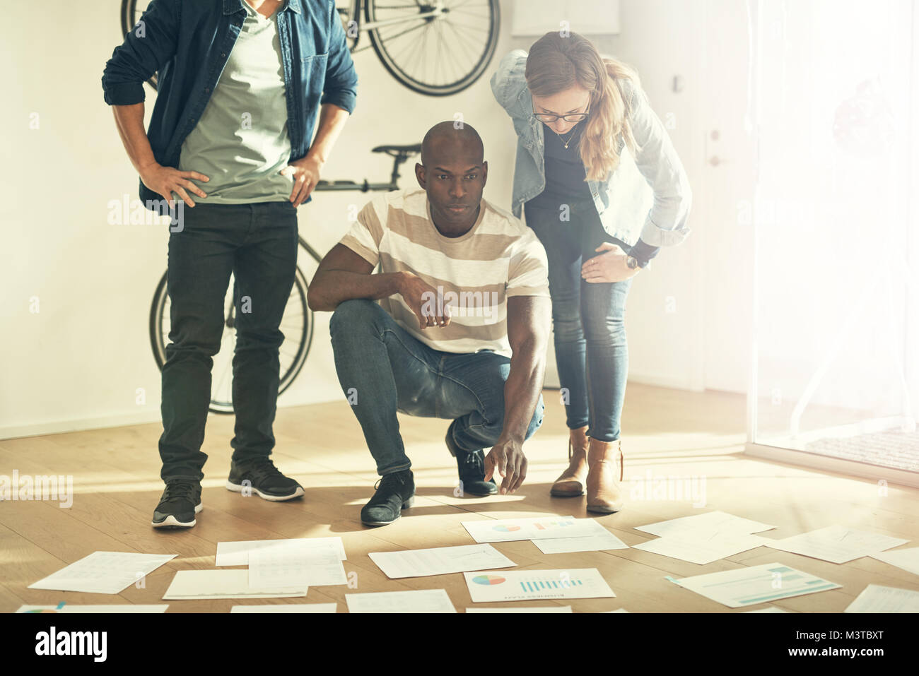Three diverse coworkers standing in stylish modern office going over ...